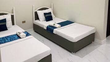 Quarto de hotel com duas camas de solteiro, cada uma com colchão branco, cabeceira escura e detalhe azul.