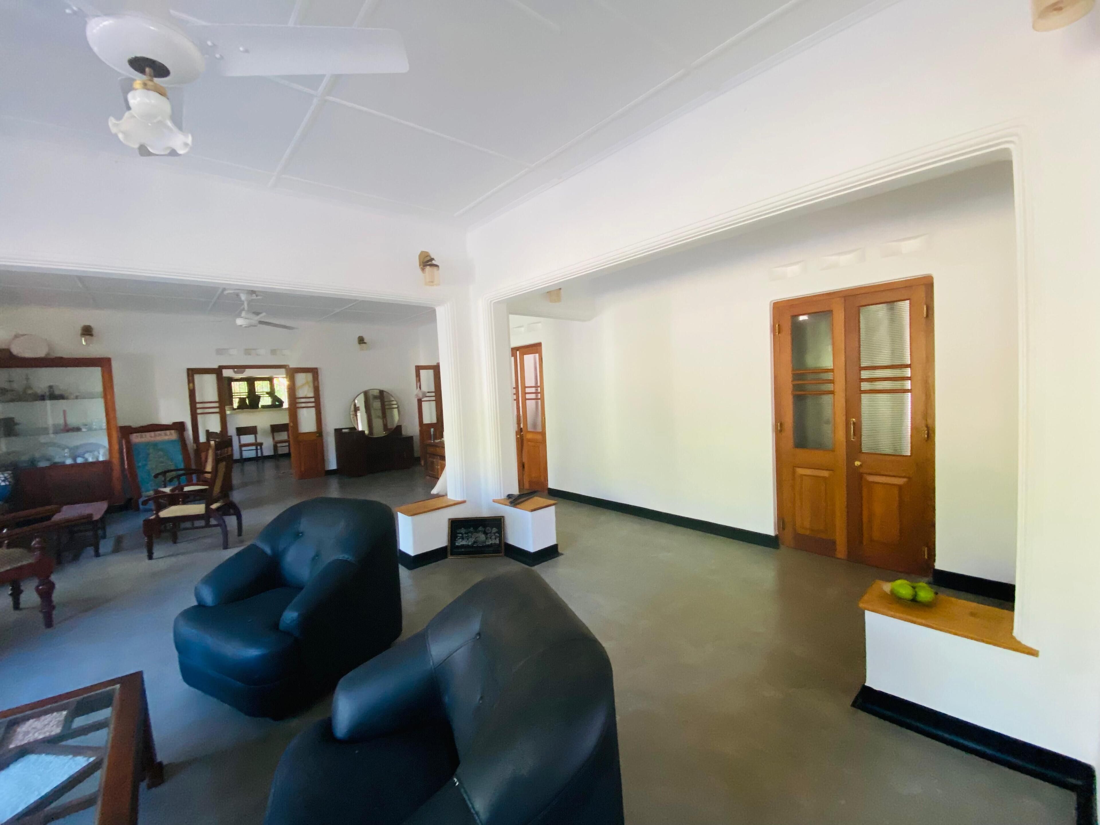 Uma sala de estar espaçosa com teto alto, ventilador de teto e porta de madeira com painéis de vidro.