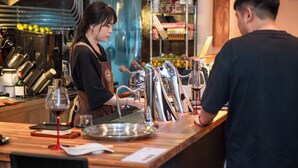 Um balcão de bar com um bartender, um cliente e diversos equipamentos de bar.