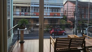 Quarto com um banco de madeira e uma mesa, porta de vidro que dá para o exterior e vista para edifícios e uma rua.