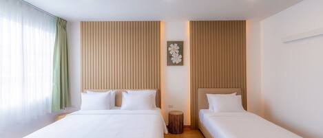 Quarto de hotel com duas camas, parede de painéis de madeira, uma pequena mesa redonda e uma janela com cortinas translúcidas.