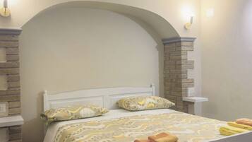 Quarto com cama branca, roupa de cama estampada e duas luminárias fixadas na parede.