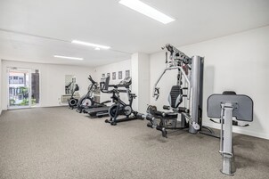 Uma academia com aparelhos de cardio, equipamentos de musculação e uma porta que dá para uma varanda.