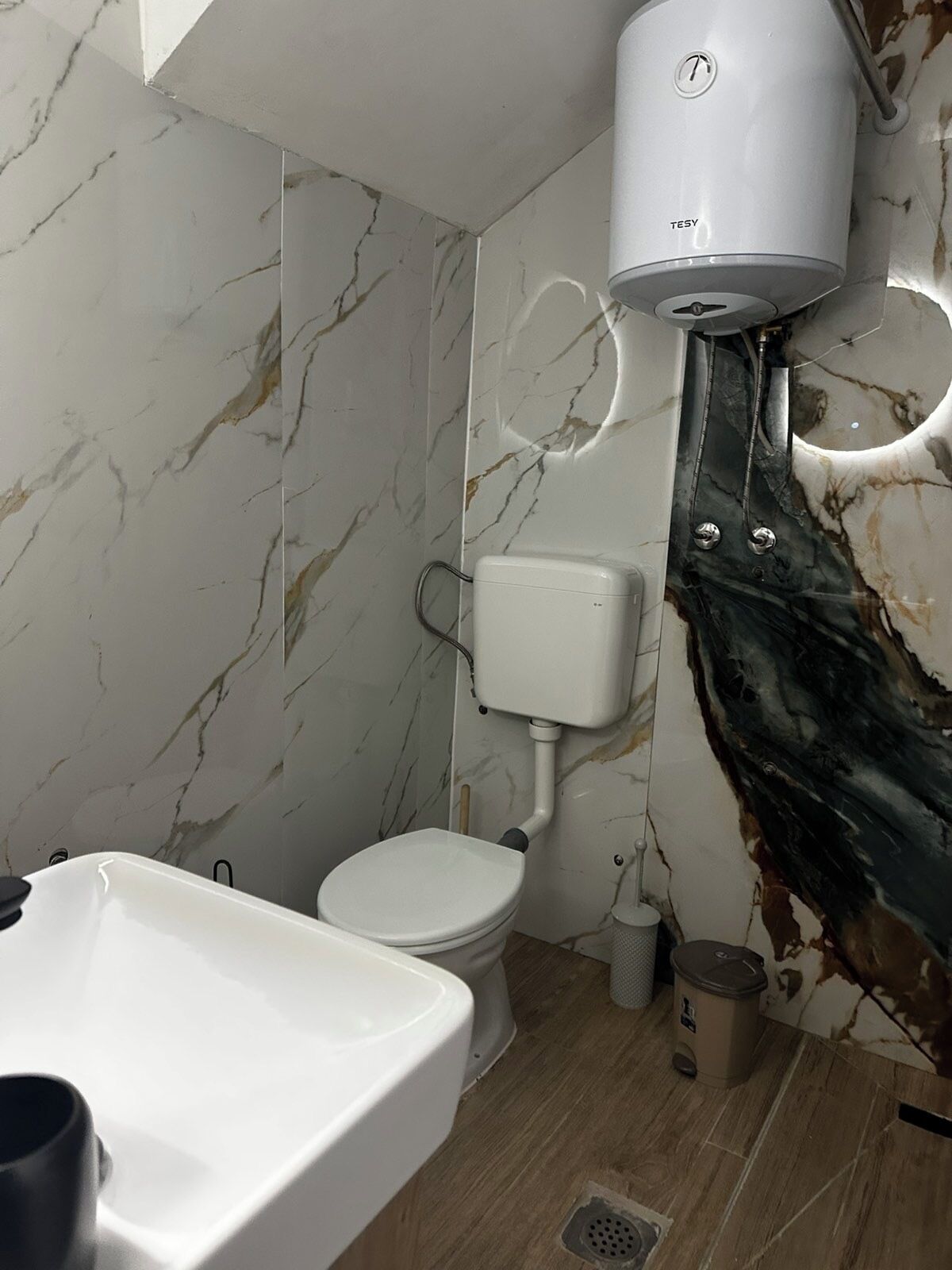 Casa de banho com sanita, lavatório e termoacumulador fixado na parede.