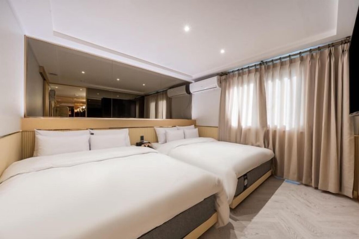 Quarto de hotel com duas camas, um espelho grande e uma janela com cortinas.
