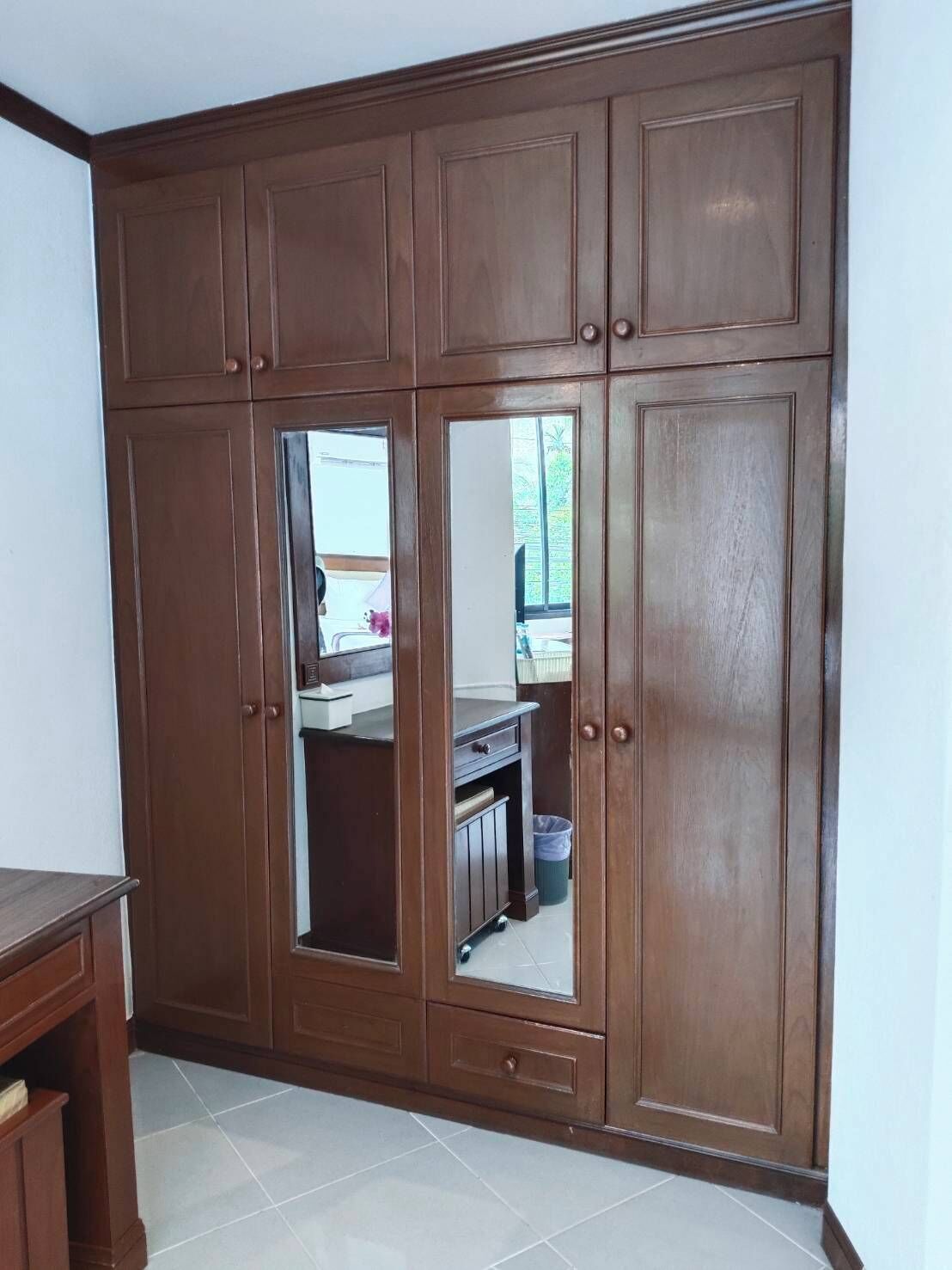 Quarto com um guarda-roupa de madeira grande, um espelho e uma pequena escrivaninha com uma cadeira.