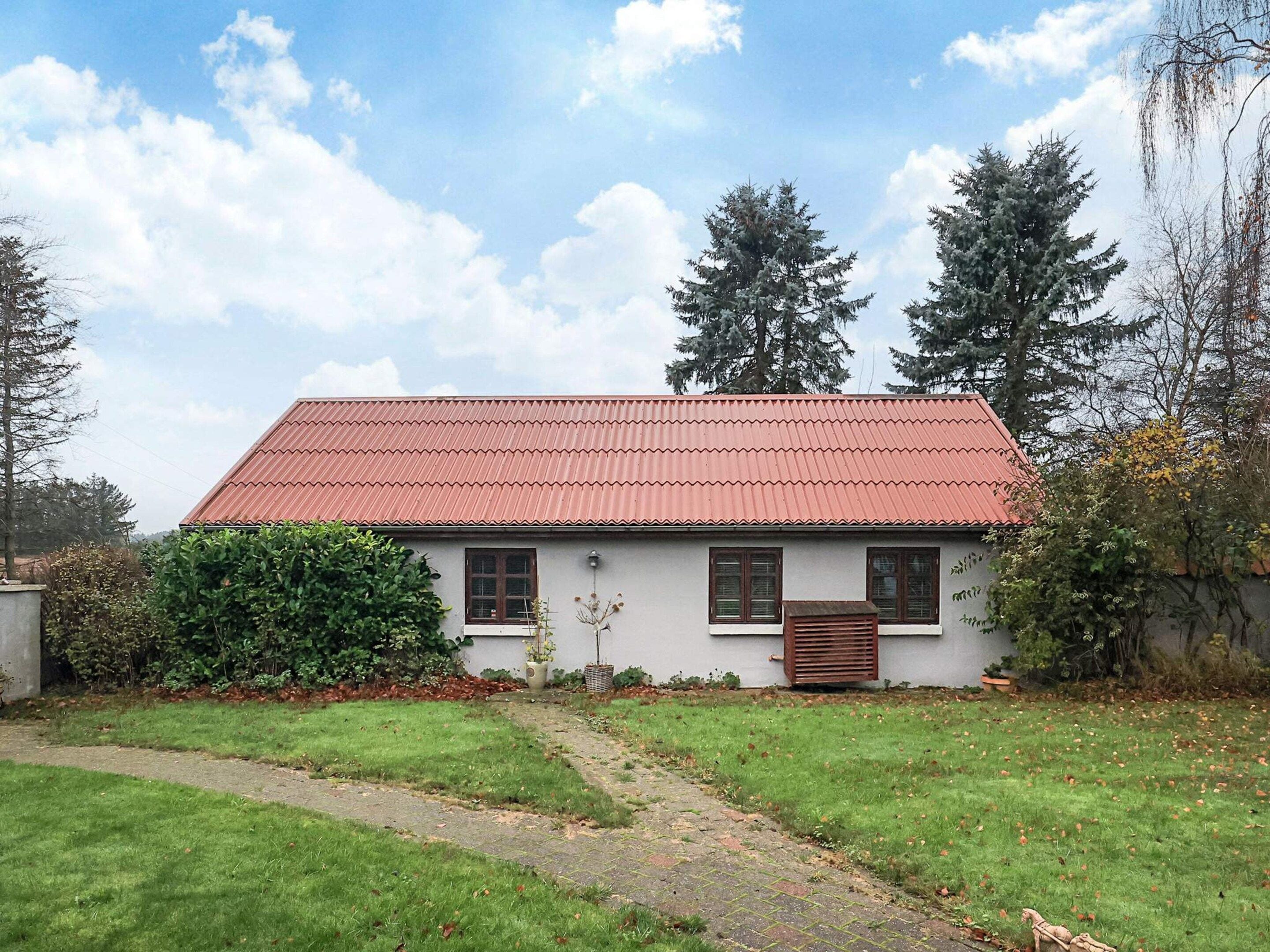Uma casa térrea com telhado de telhas vermelhas, varanda frontal e um caminho que leva à entrada.