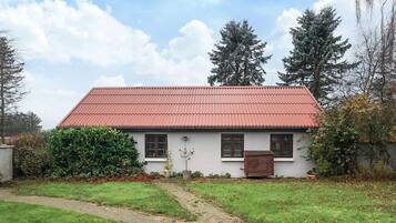 Uma casa térrea com telhado de telhas vermelhas, varanda frontal e um caminho que leva à entrada.