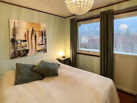 Quarto de hotel com uma cama grande, um candelabro, um quadro na parede e uma janela com cortinas.