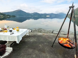 Mesa posta com itens de café da manhã e lareira suspensa à beira de um lago.