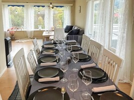 Mesa de jantar posta com pratos, copos e talheres, rodeada por cadeiras brancas.