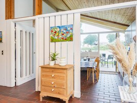 Quarto com cômoda de madeira, pintura de flores e vista para um pátio externo com cadeiras e mesa.