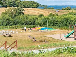 Um parque com mesas de piquenique, parquinho infantil e uma vista panorâmica da água.