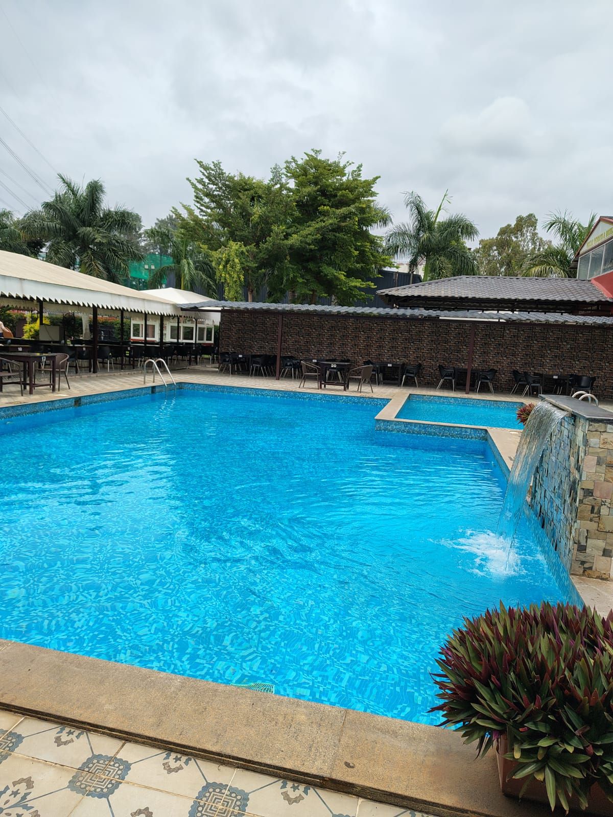 Piscina com cachoeira artificial, rodeada por espreguiçadeiras e área de estar coberta.