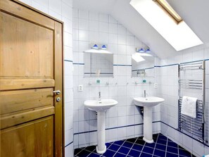 Casa de banho com duas pias, porta de madeira, paredes com azulejos brancos e chão azul.