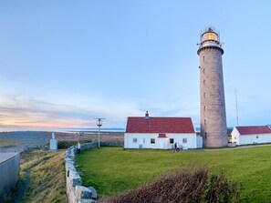 Um farol com telhado vermelho, torre de pedra e um edifício branco com telhado vermelho.