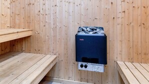 Uma sauna com bancos de madeira e um aquecedor preto com a etiqueta 'helo' e um painel de controle.