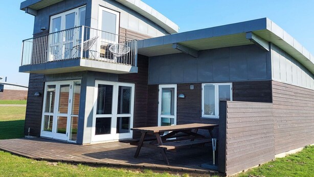 Uma casa moderna de dois andares com varanda, janelas amplas e deck de madeira.