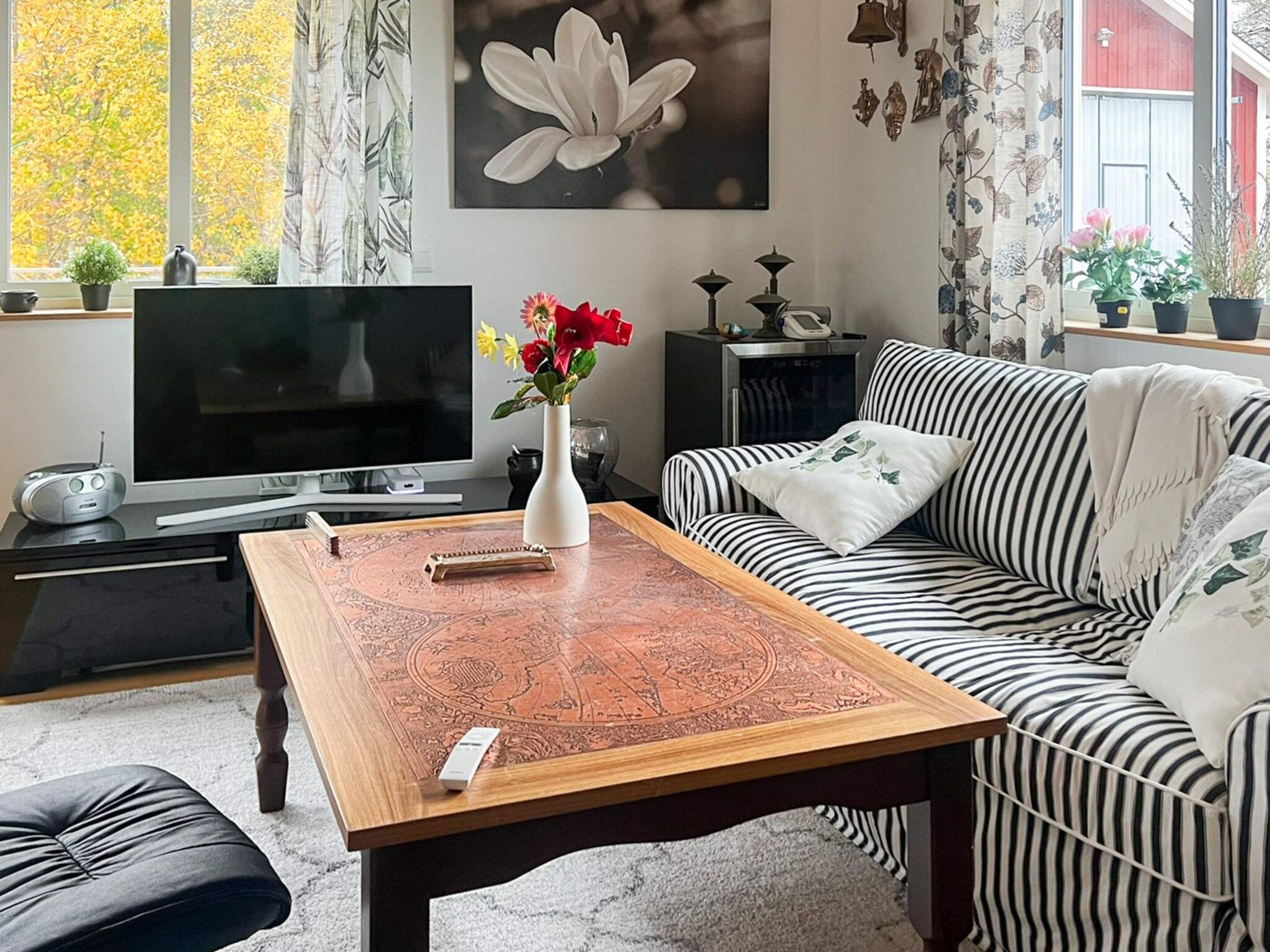 Sala de estar com televisão, sofá, mesa de centro e um vaso decorativo com flores.