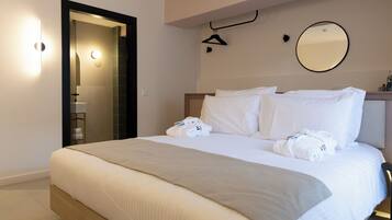Quarto de hotel com uma cama grande, uma mesa de cabeceira, um espelho e um porta-toalhas fixado na parede.