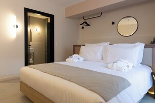 Quarto de hotel com uma cama grande, uma mesa de cabeceira, um espelho e um porta-toalhas fixado na parede.