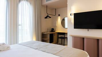 Quarto de hotel com cama, escrivaninha, cadeira, televisão e banheiro com cortina de chuveiro.