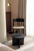 Quarto moderno com uma cadeira preta, uma mesa pequena, um abajur e uma janela com cortinas.