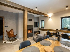 Uma sala de jantar moderna com uma mesa de madeira, jogos americanos cinzas e uma lareira.