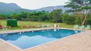 Piscina com vista clara para montanhas ao fundo, rodeada por um espaço de estar com cadeiras e área coberta.