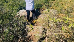 Uma pessoa em uma formação rochosa com os braços estendidos, contemplando uma paisagem montanhosa.