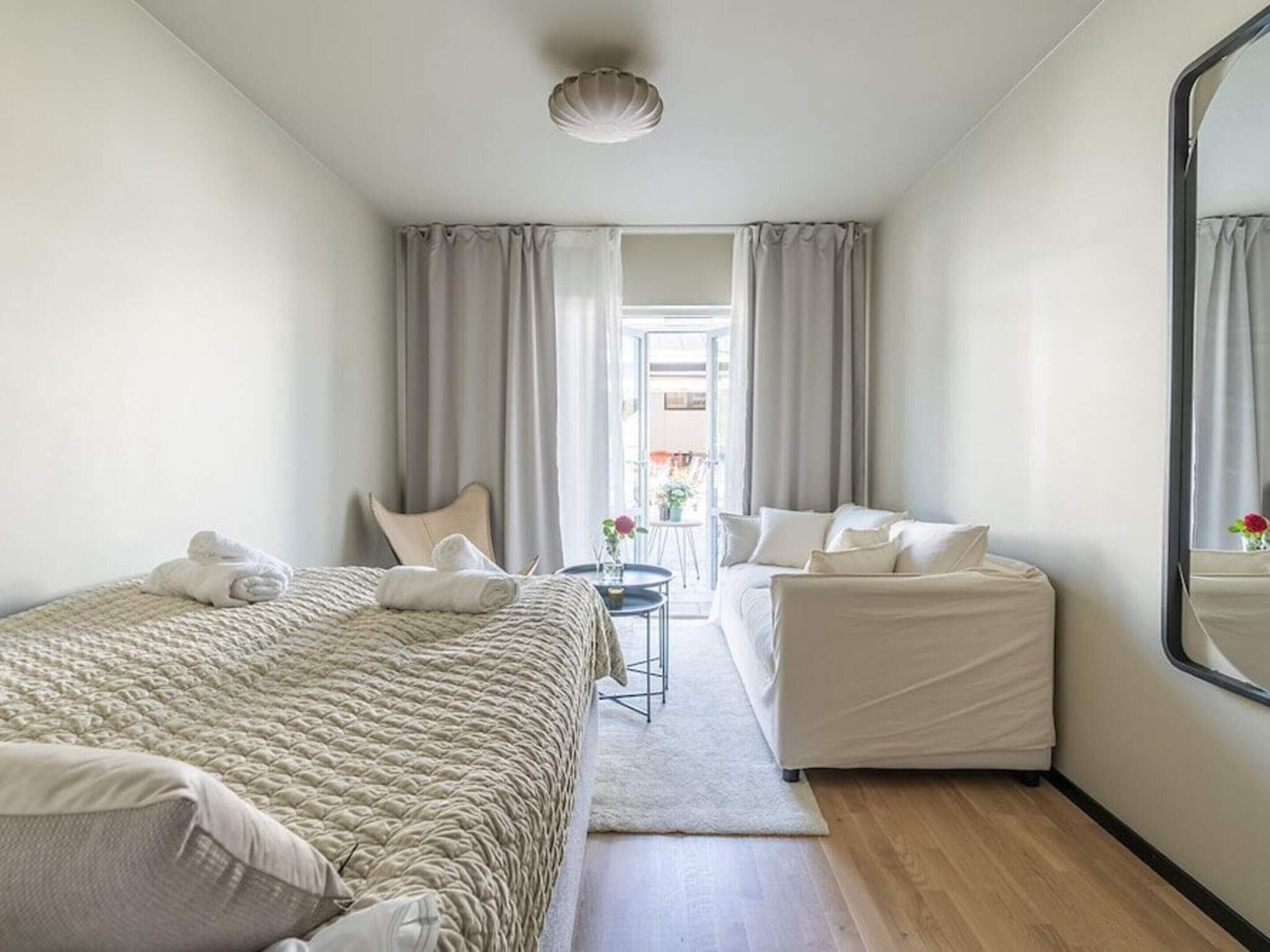 Quarto de hotel com cama, sofá, uma mesinha e espelho.