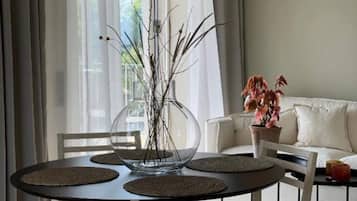 Uma área de refeições com uma mesa redonda, cadeiras brancas e um vaso com ramos.