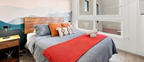Quarto com cama, mesa de cabeceira, luminária e janela com vista.