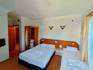 Quarto de hotel com duas camas, um guarda-roupa, mesa de cabeceira com abajur e um pequeno frigorífico.