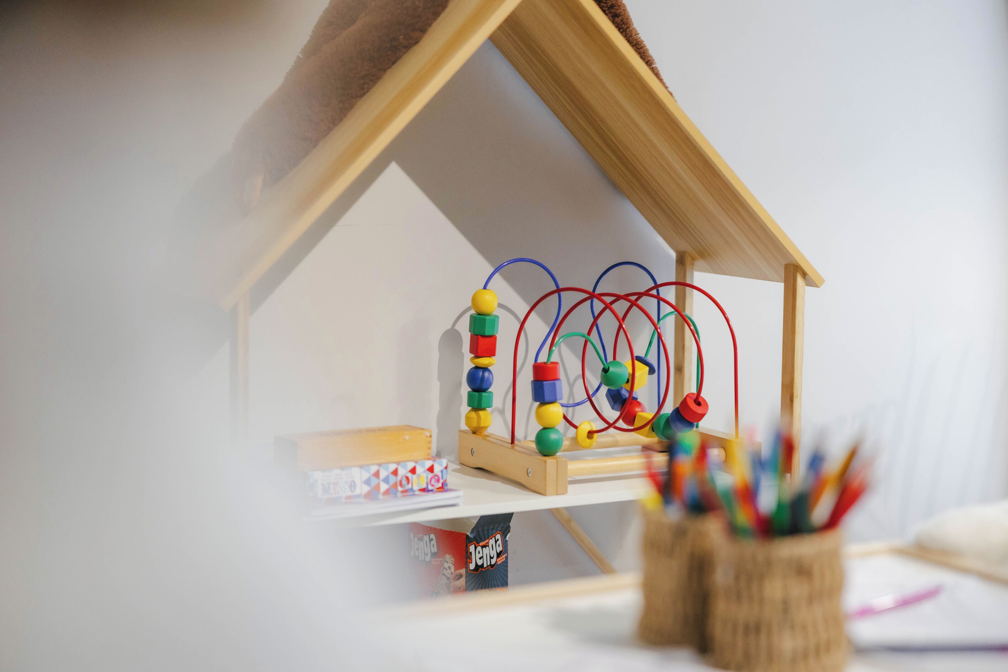 Um modelo de casa de madeira com contas coloridas e fios, uma caixa de giz de cera e um recipiente com blocos de Jenga.