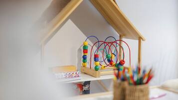 Um modelo de casa de madeira com contas coloridas e fios, uma caixa de giz de cera e um recipiente com blocos de Jenga.