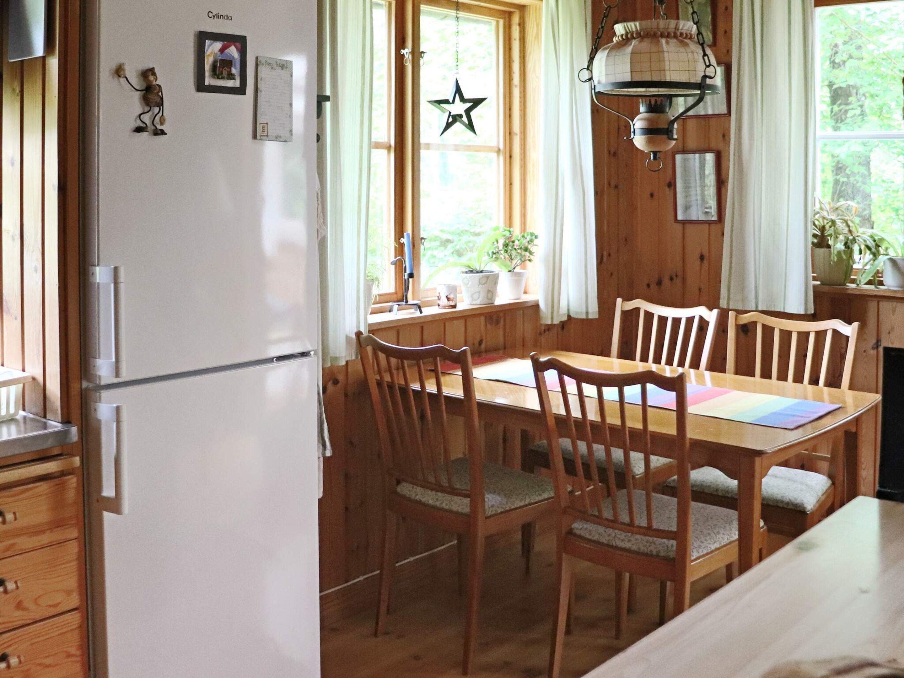 Uma mesa de jantar de madeira com cadeiras, um refrigerador branco e um lustre.