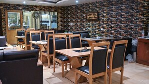 Um restaurante com mesas de madeira e cadeiras estofadas pretas, parede estampada e um relógio na parede.