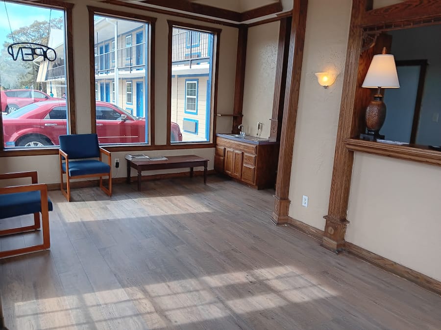 Um quarto espaçoso com grandes janelas, um banco de madeira, uma pequena mesa e uma área de cozinha com armários de madeira.