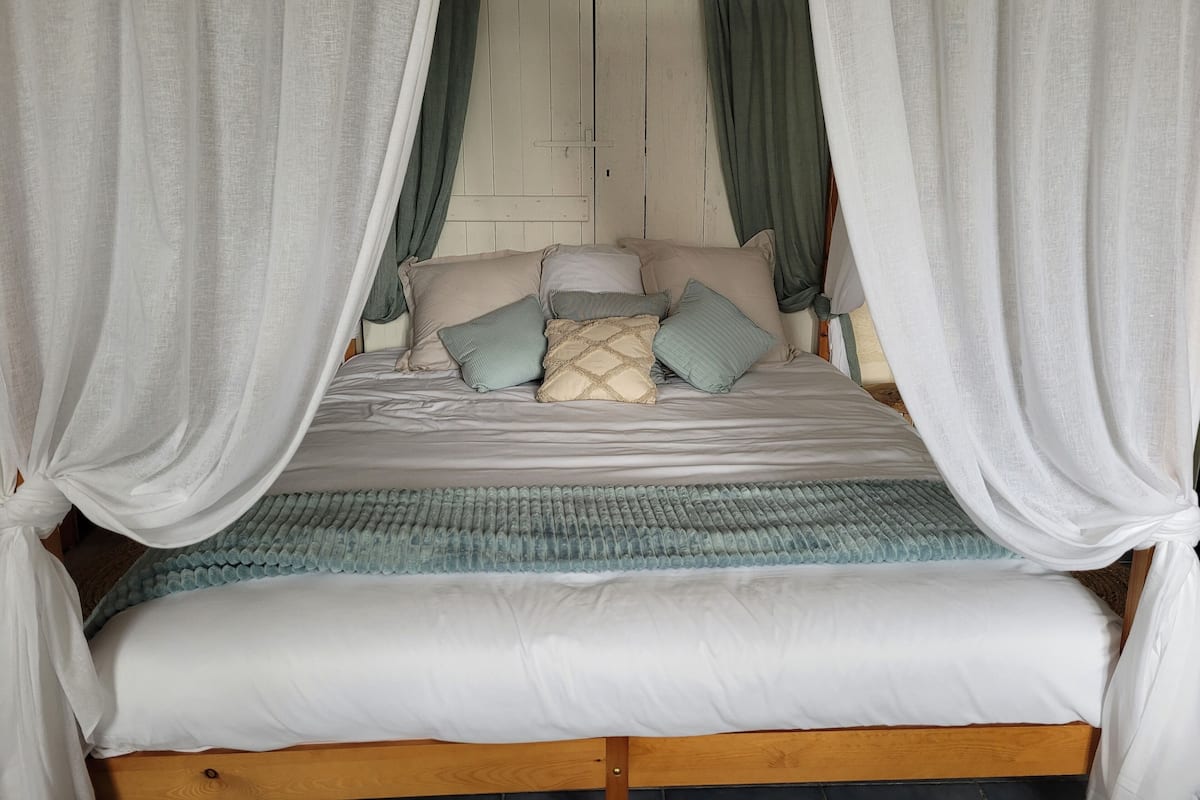 Uma cama com dossel, almofadas e colcha.