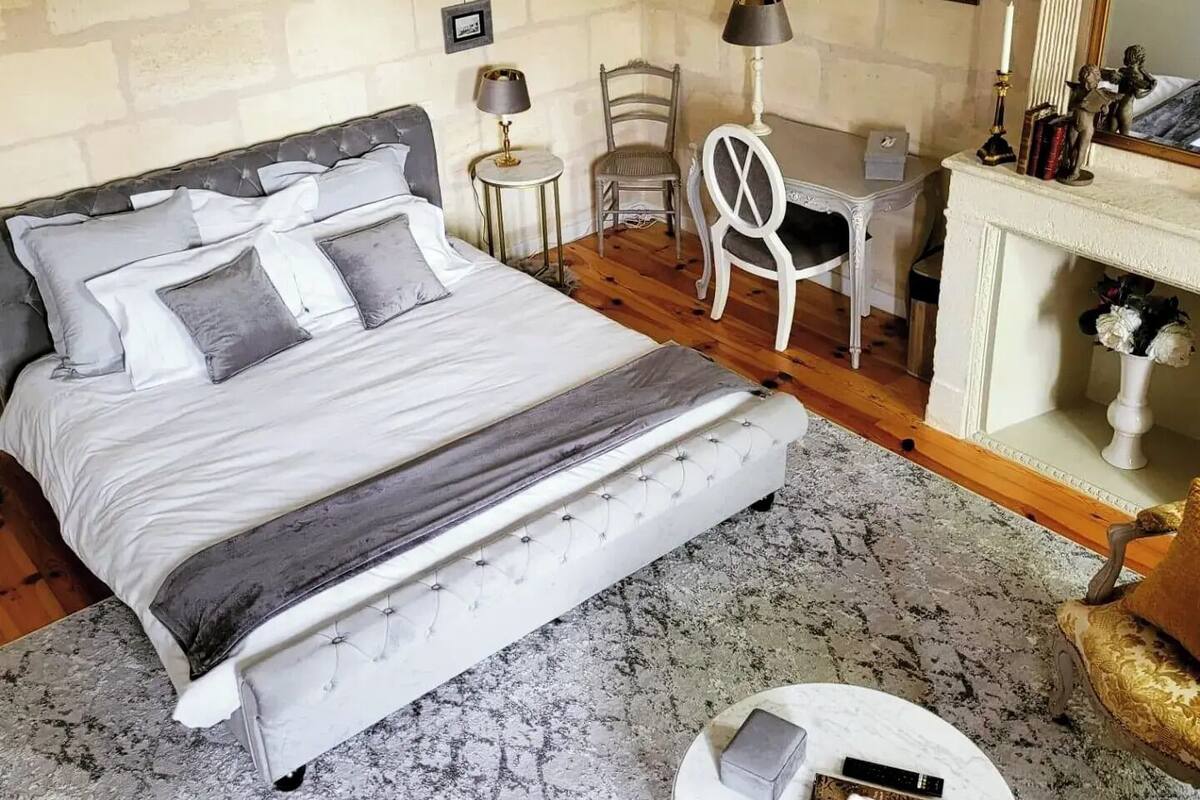 Quarto com cama, escrivaninha, cadeira, lareira e um quadro na parede.