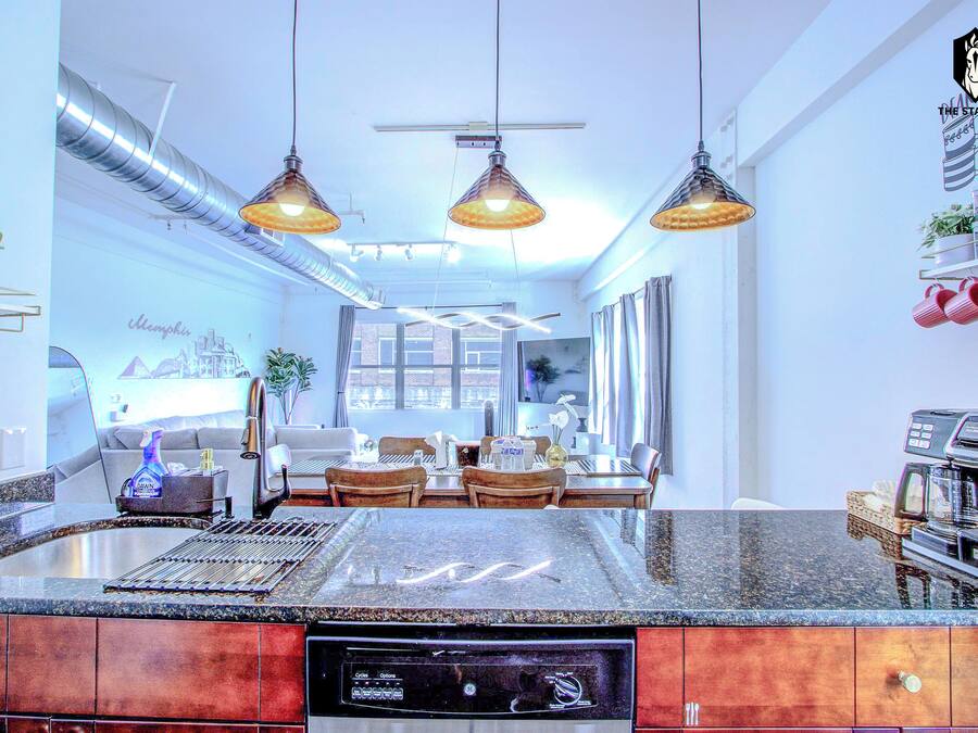 Cozinha moderna com ilha central, iluminação pendente e máquina de café.