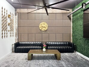Uma sala de estar moderna com um sofá de couro preto, uma mesa de centro de madeira, um ventilador de teto e um painel decorativo com um emblema de leão.