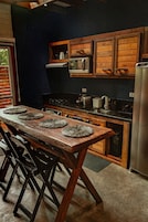 Uma cozinha com armários de madeira, uma geladeira de aço inoxidável e uma mesa de madeira comprida com jogos americanos trançados.