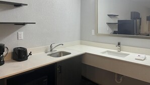 Uma casa de banho de hotel compacta, com lavatório, espelho e máquina de café.