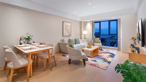 Uma sala de estar moderna com área de jantar, sofá, mesa de centro e uma grande janela com vista para a cidade.