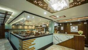 Uma área de recepção de hotel com balcão de mármore, vitrines de vidro e um candelabro.