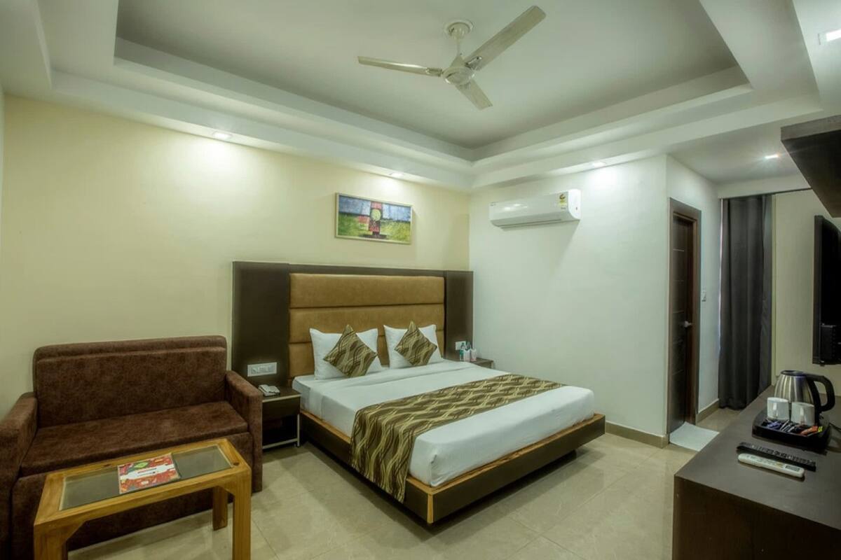 Quarto de hotel com cama, sofá, mesa de centro, televisão e ventoinha no teto.