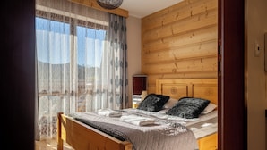 Quarto com painéis de madeira, uma cama, uma janela com cortinas leves e piso de madeira.