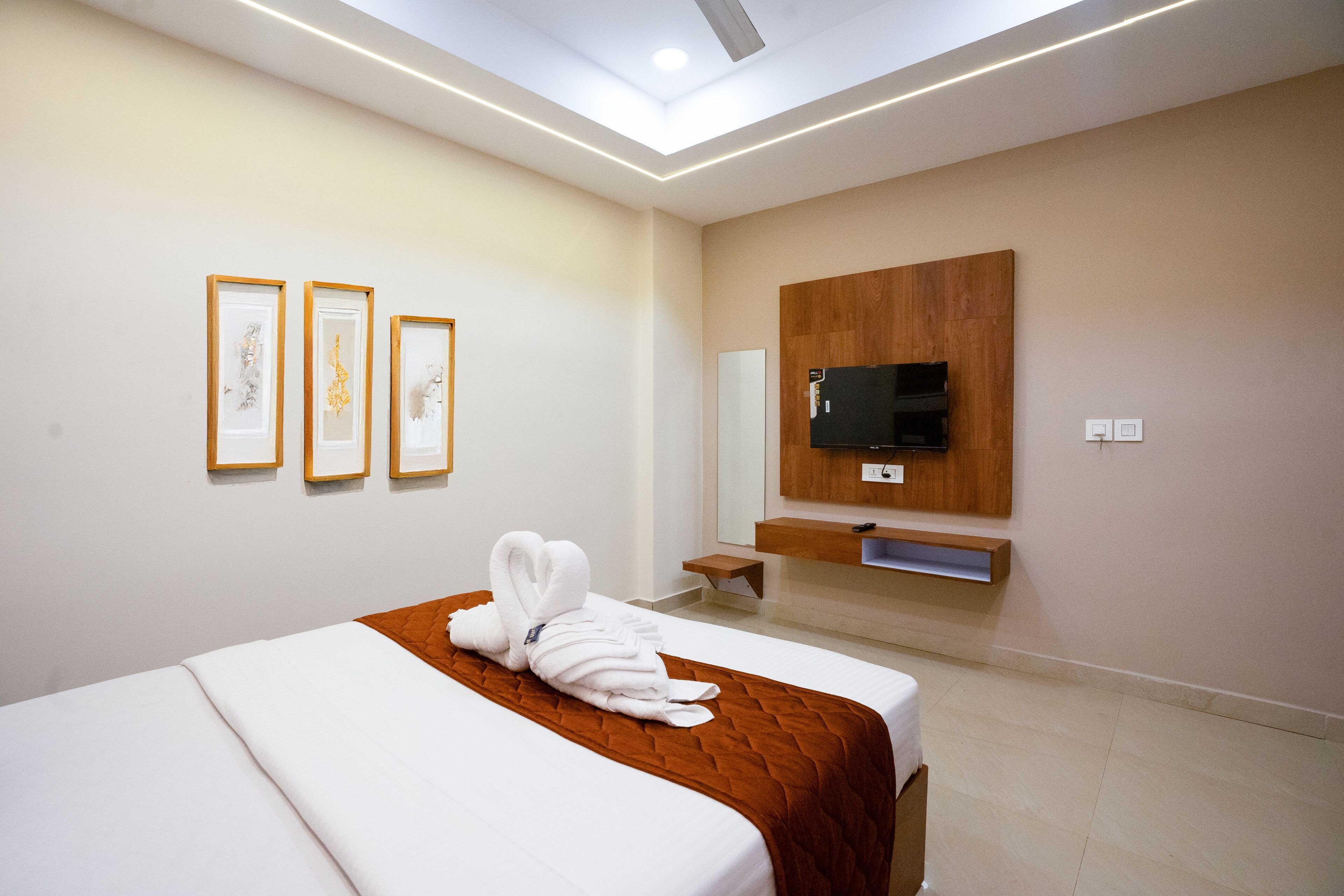 Quarto de hotel moderno com uma cama bem arrumada, uma televisão de tela plana na parede e três obras de arte emolduradas na parede.